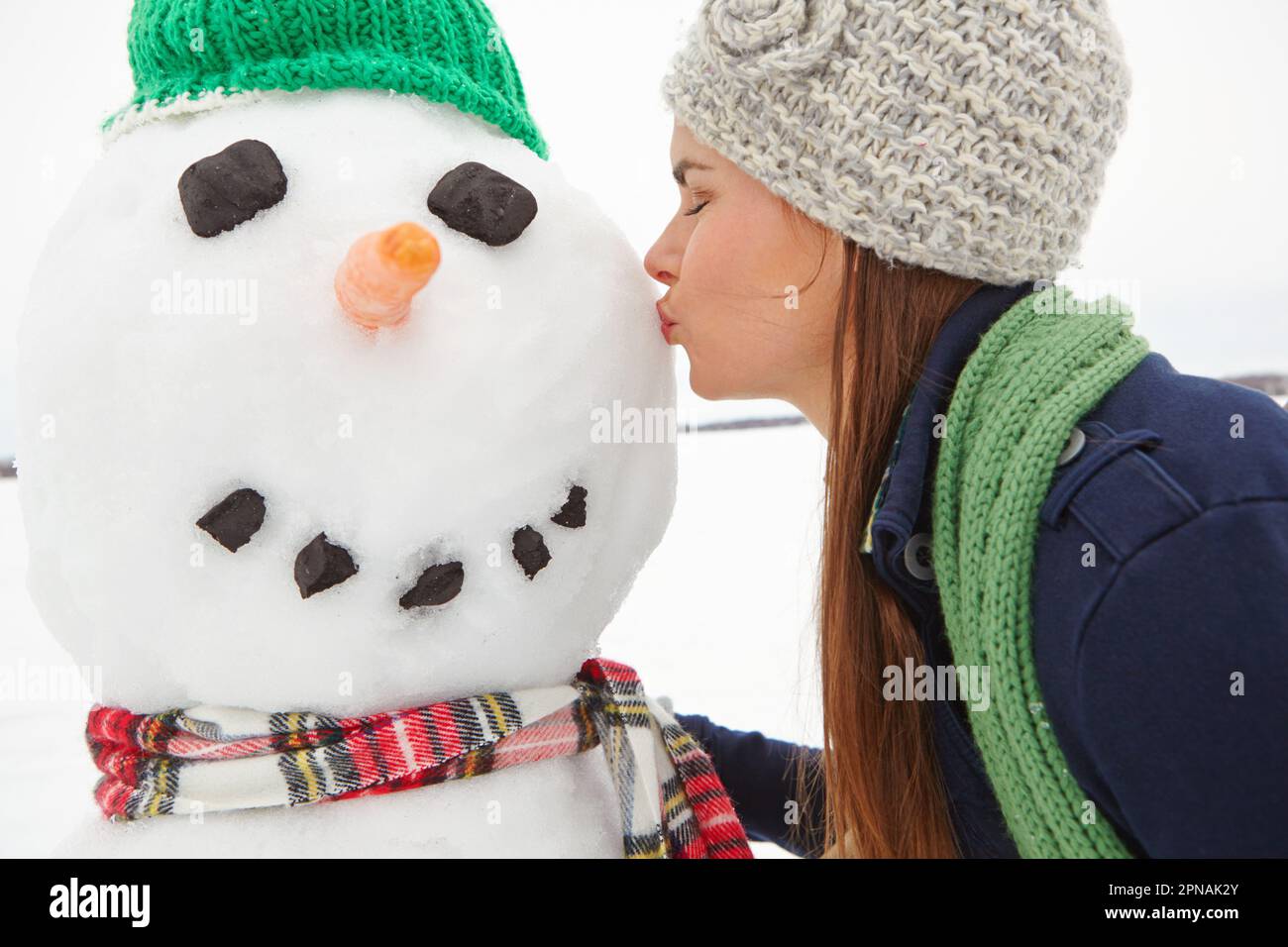 Giving the snowman a little sugar. a beautiful young woman kissing a ...
