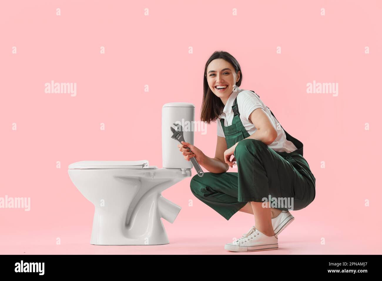 Female plumber with wrench and toilet bowl on pink background Stock ...
