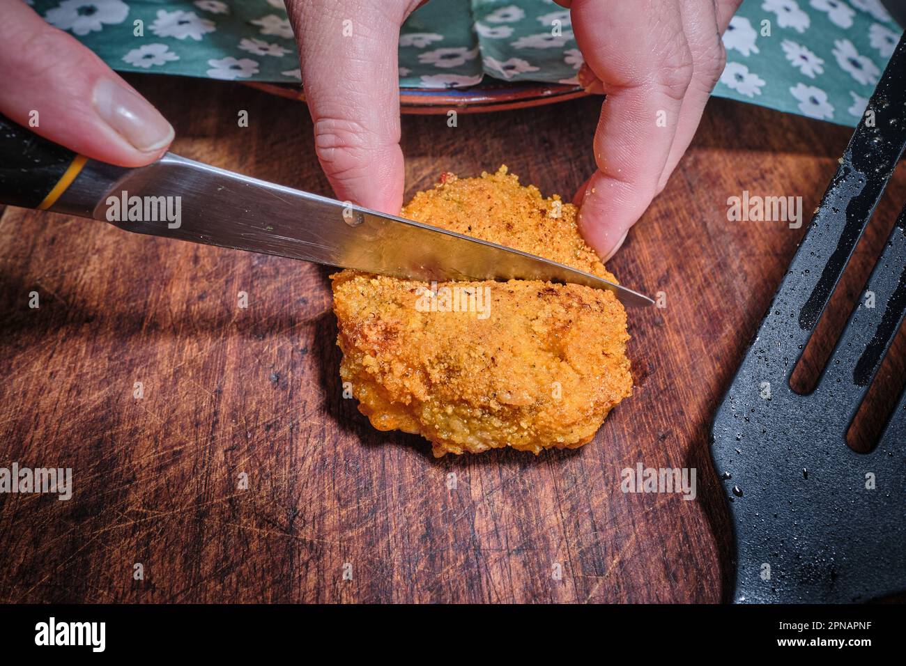 Hands hold a tasty freshly cooked cutlet/patty and a knife cutting it ...