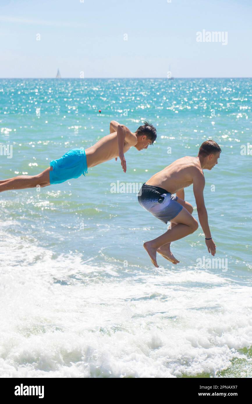 teenage boys in swimming shorts jumping into the sea from a pier in ...