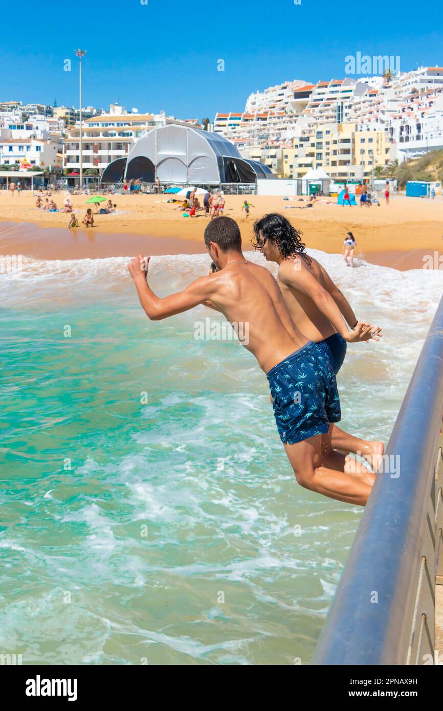 teenage boys in swimming shorts jumping into the sea from a pier in ...