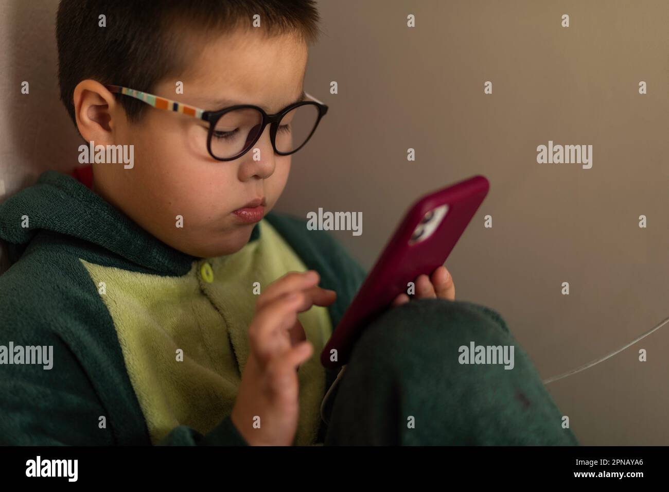 Closeup portrait of a boy who looks into the phone sitting at the table ...