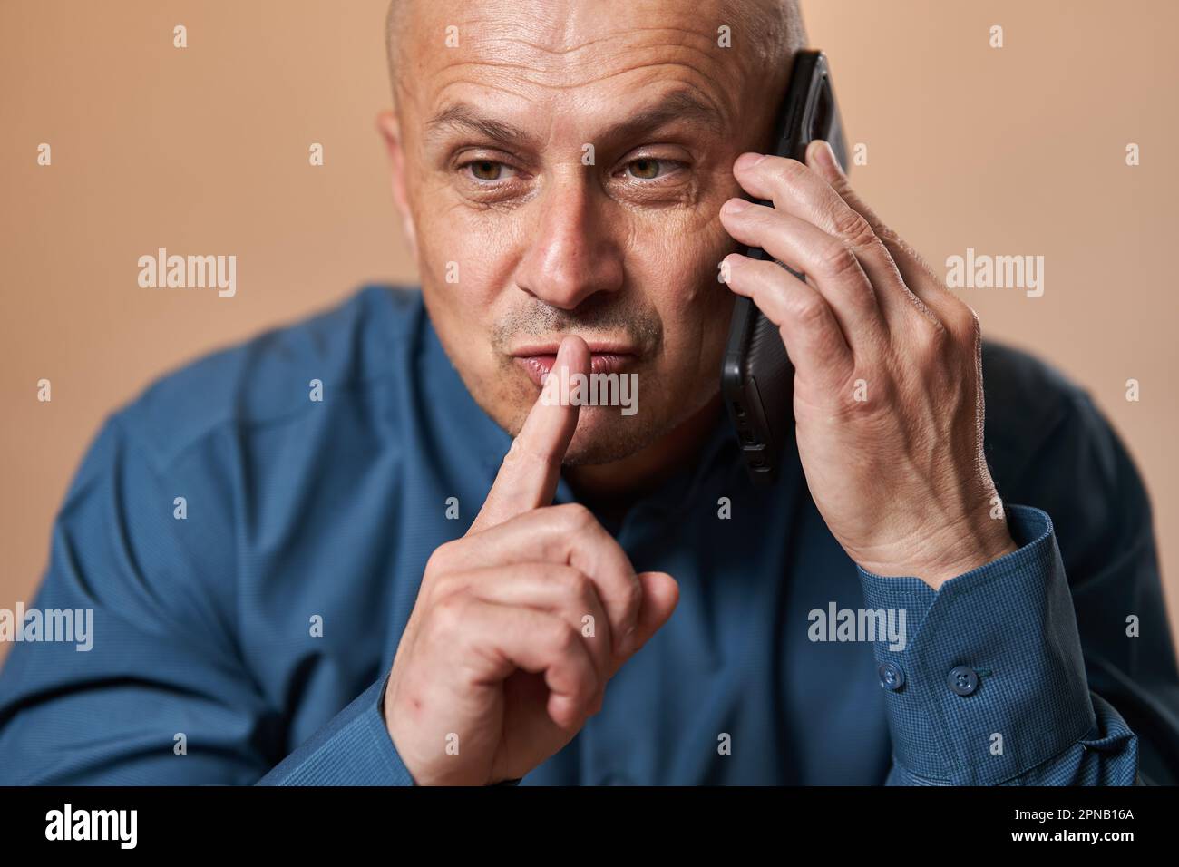 Mature businessman telling a secret in a phone conversation, over fawn ...