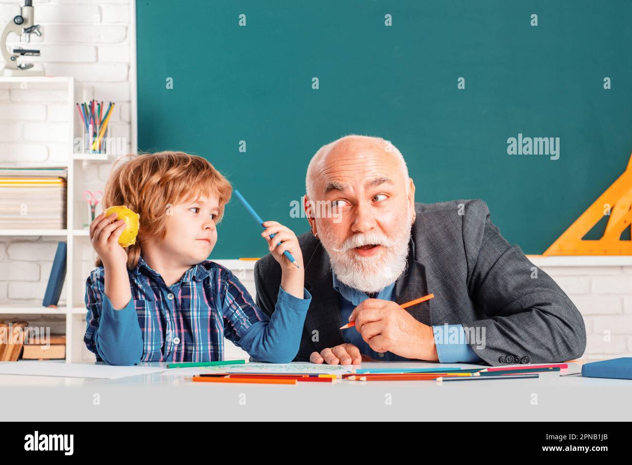 Mature man teacher and pupil on balckboard background. Senior teacher ...