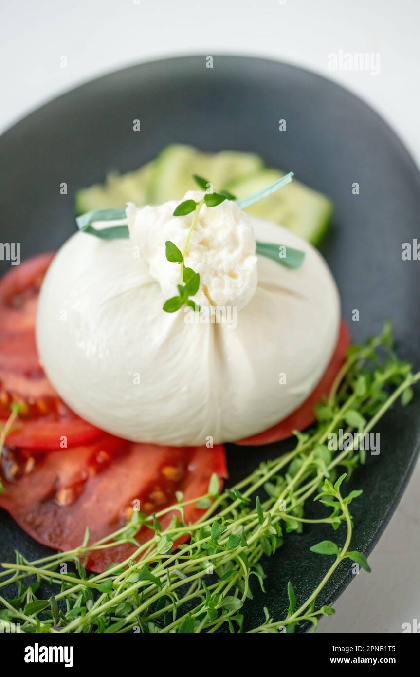 Italian cheese burrata, tomatoes and vegetables close-up. A layer of ...