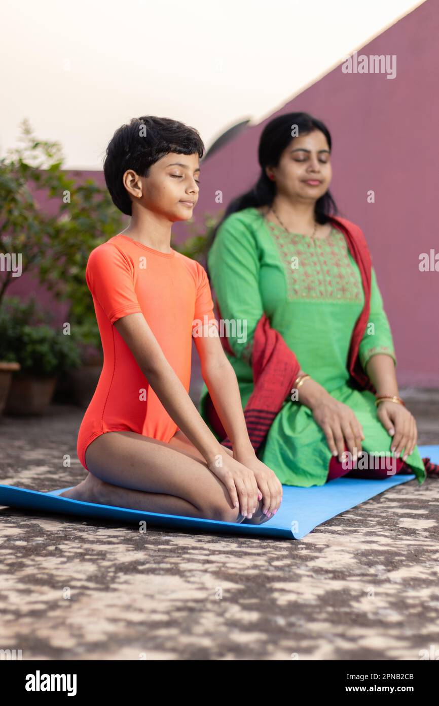 An Indian girl child with mother practicing Vajrasana yoga on yoga mat ...