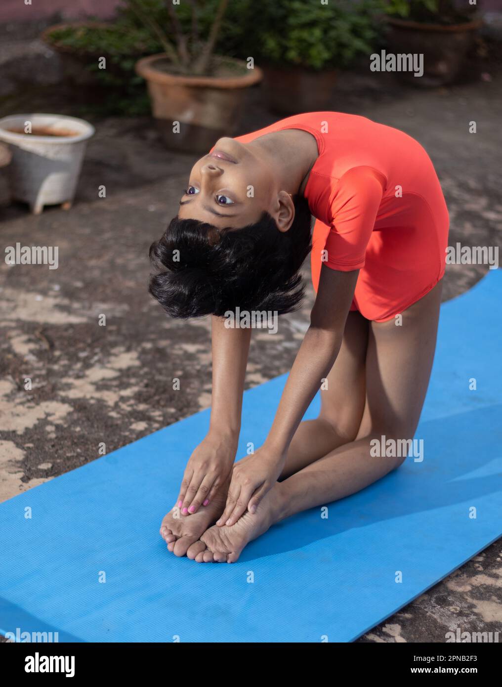 An Indian girl child practicing Ustrasana yoga on yoga mat outdoors ...