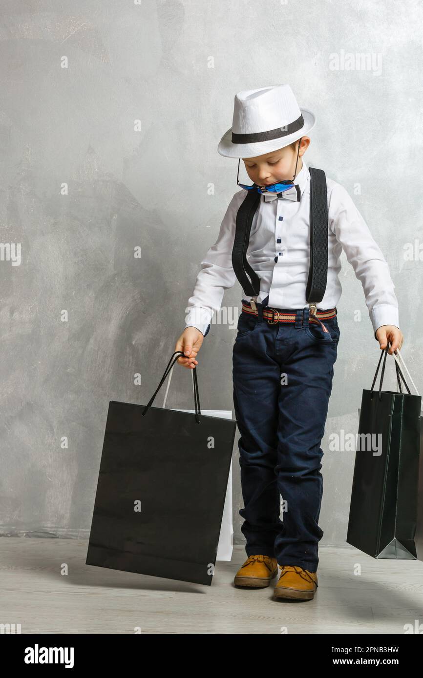 charming little boy go shopping show bags buy casual clothes on gray ...