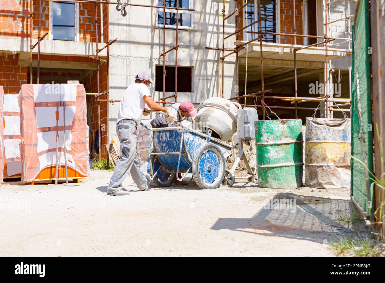 Teamwork, workers are pouring fresh mortar in wheelbarrow from mortar ...