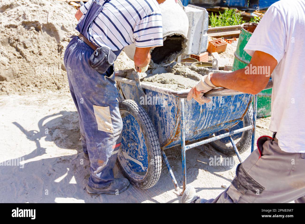 Teamwork, workers are pouring fresh mortar in wheelbarrow from mortar ...