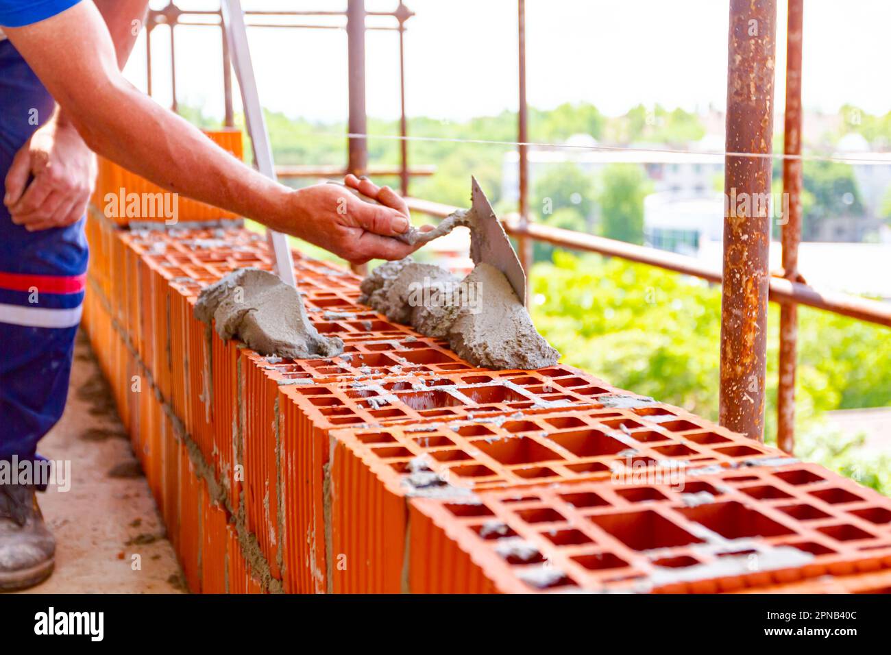 Worker is using spatula, trowel, to apply mortar on red blocks to make ...