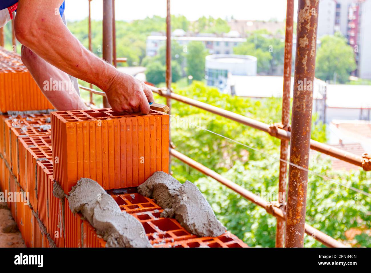 Mason, bricklayer worker is using red blocks to mount a wall next the ...