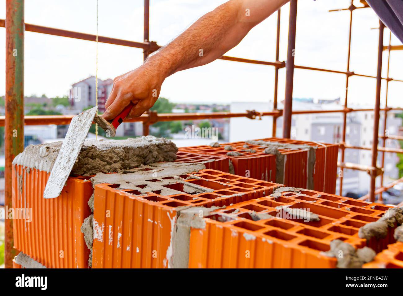 Worker is using spatula, trowel, to apply mortar on red blocks to make ...
