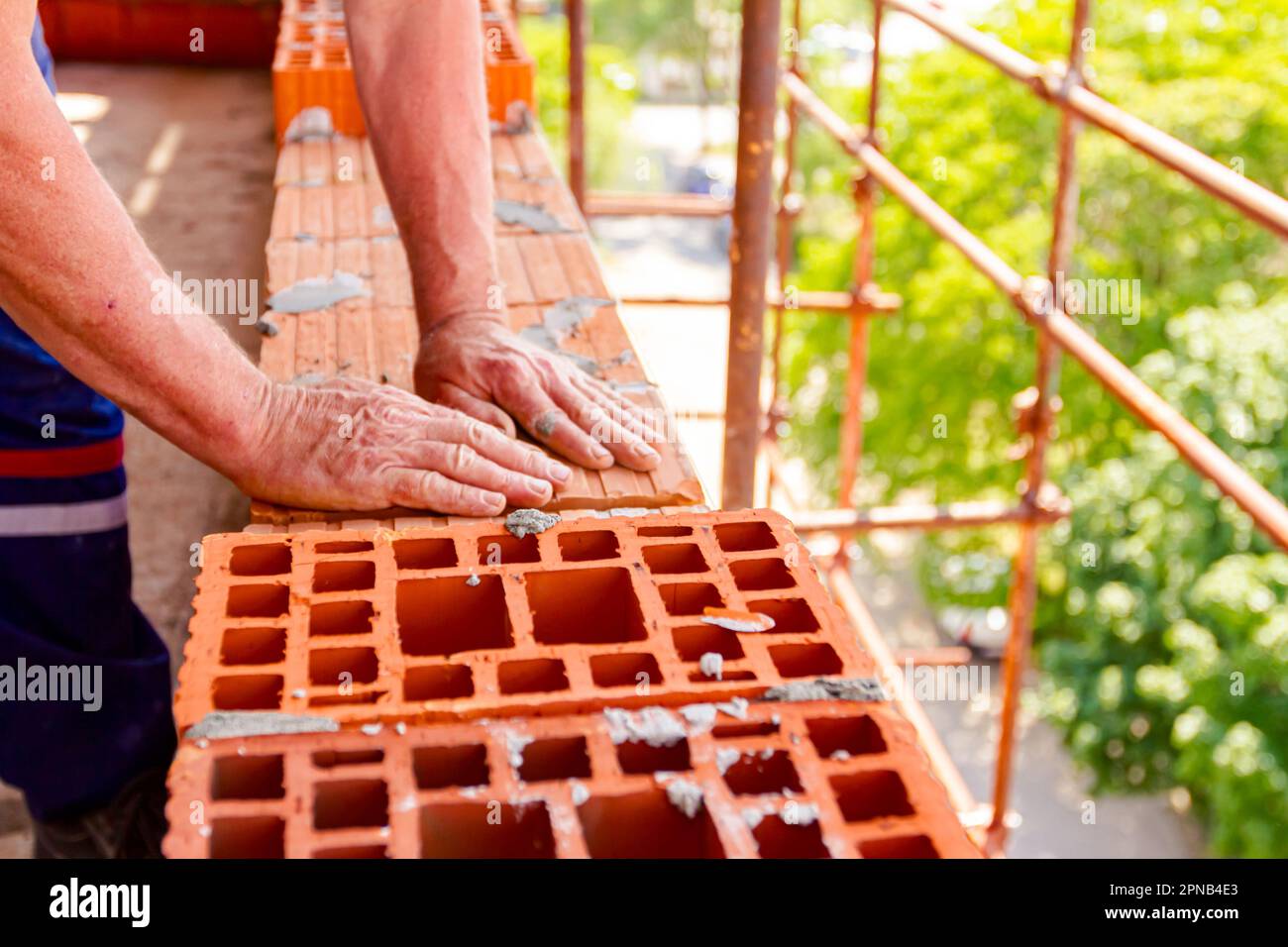 Mason, bricklayer worker is using red blocks to mount a wall next the ...