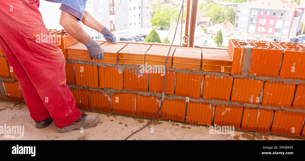 Mason, bricklayer worker is using red blocks to mount a wall next the ...
