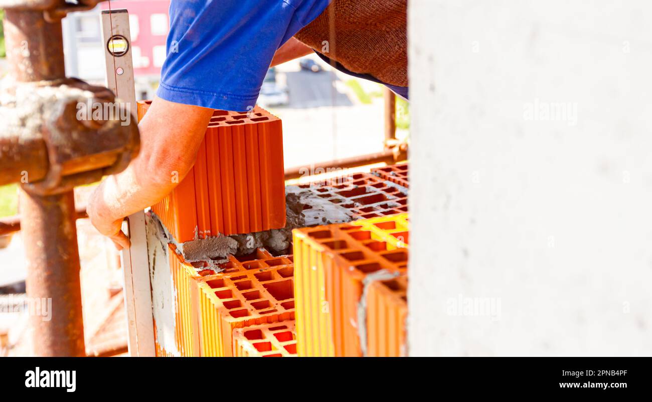 Builder is using a spirit level to check new red brick wall made of red ...