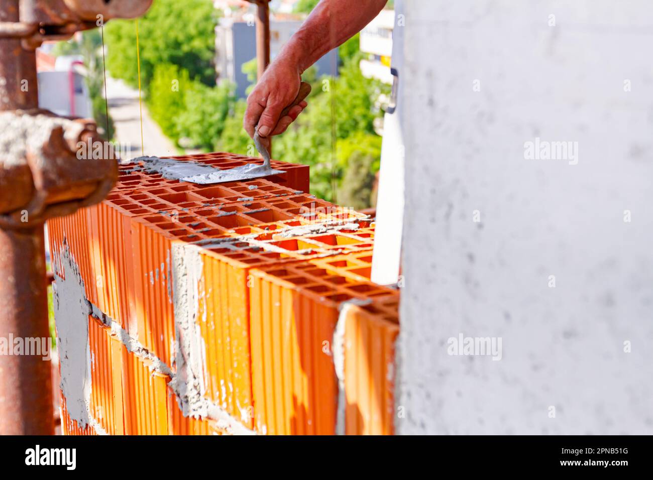 Worker holds spatula, trowel, for applying mortar on red blocks to ...