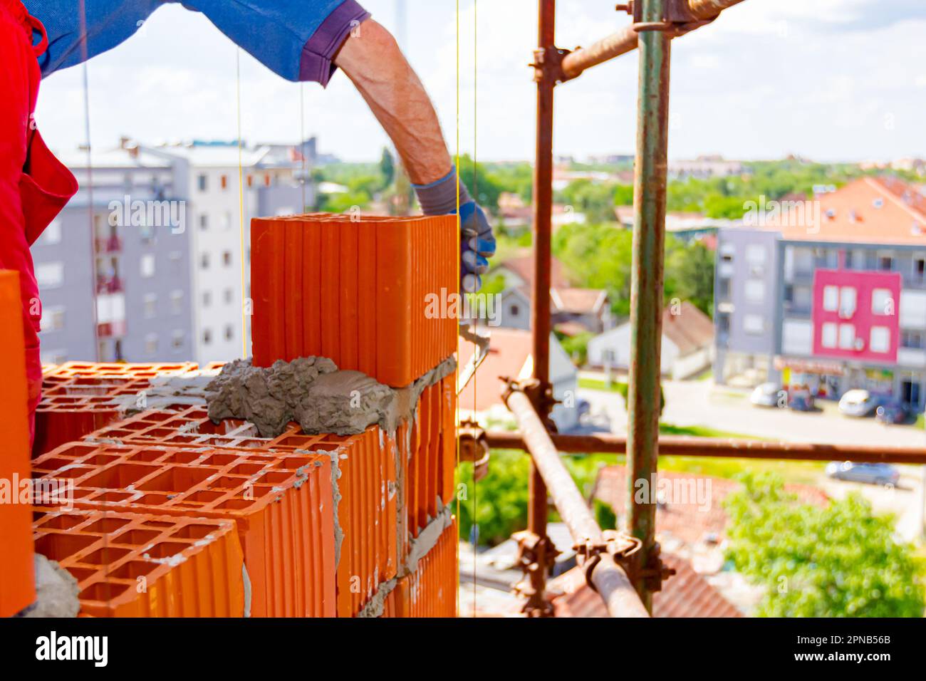 Worker holds spatula, trowel, for applying mortar on red blocks to ...