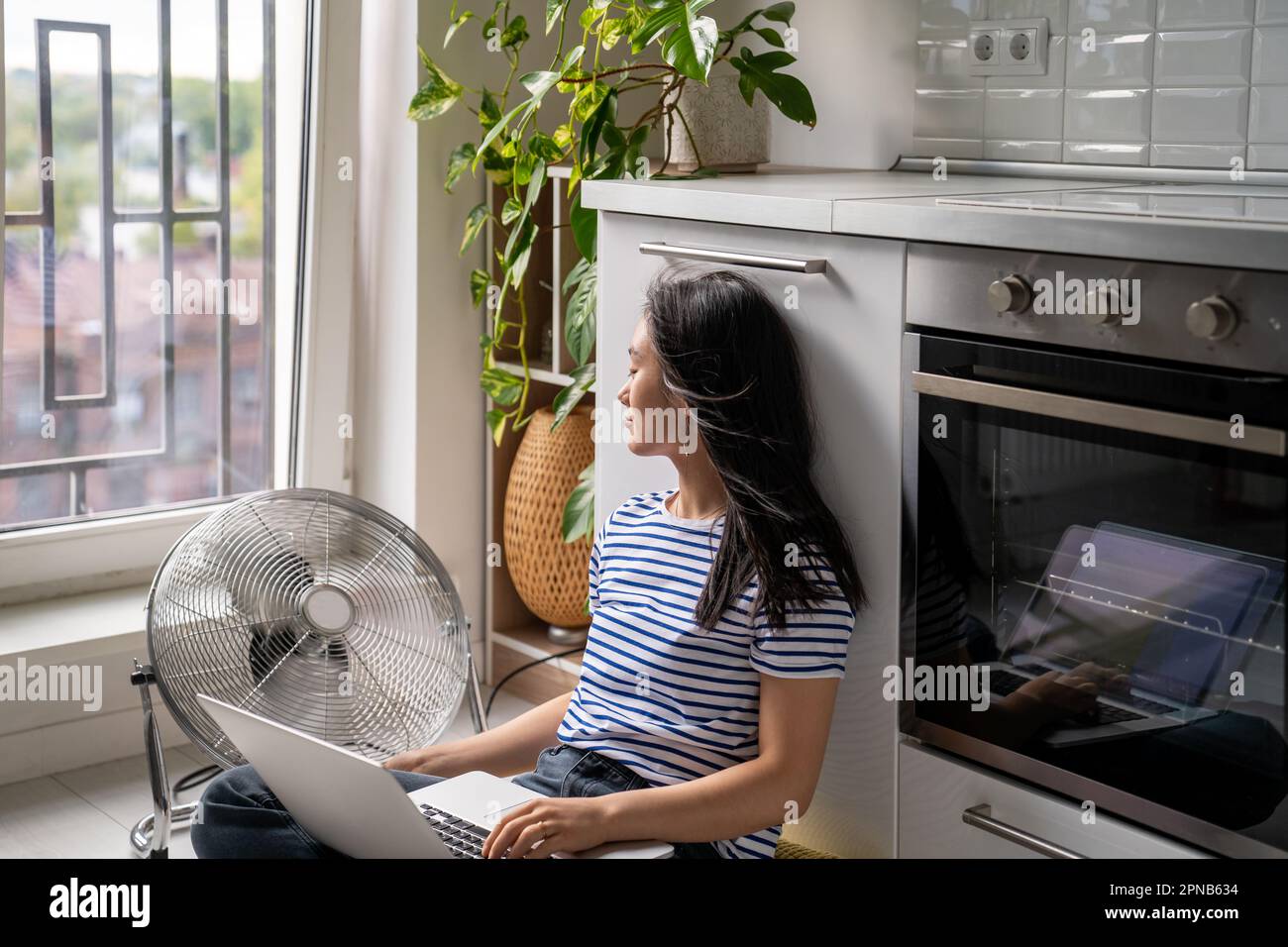 Relaxed carefree Asian woman sits on floor with laptop on lap and ...