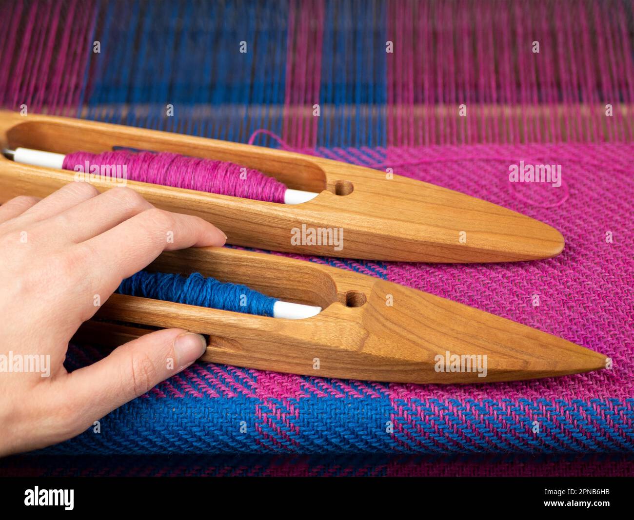 Hand takes a wooden boat shuttle with blue yarn to make a weaving ...