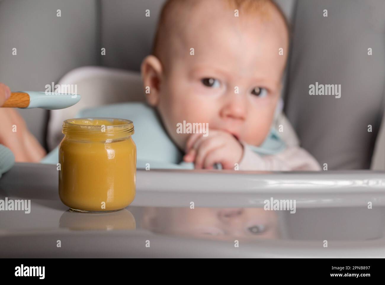 A small child 5-6 months old looks at a jar of vegetable and fruit ...