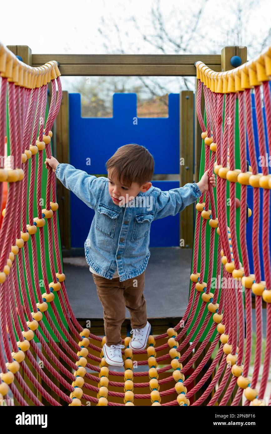 Full body of cute boy walking on rope bridge and looking away while ...