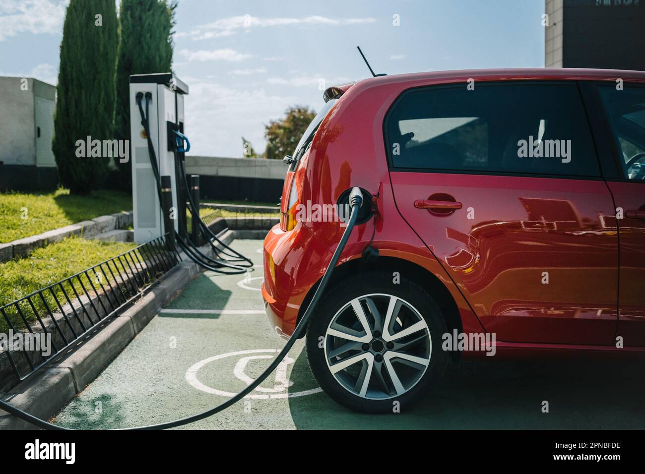 Contemporary red electric car parked on asphalt road while charging ...