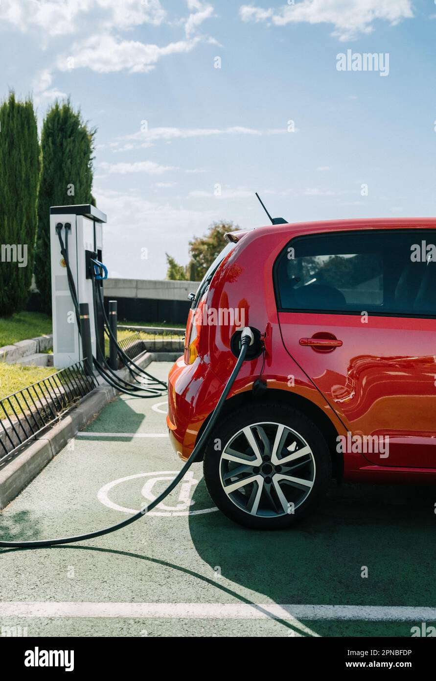 Contemporary red electric car parked on asphalt road while charging ...