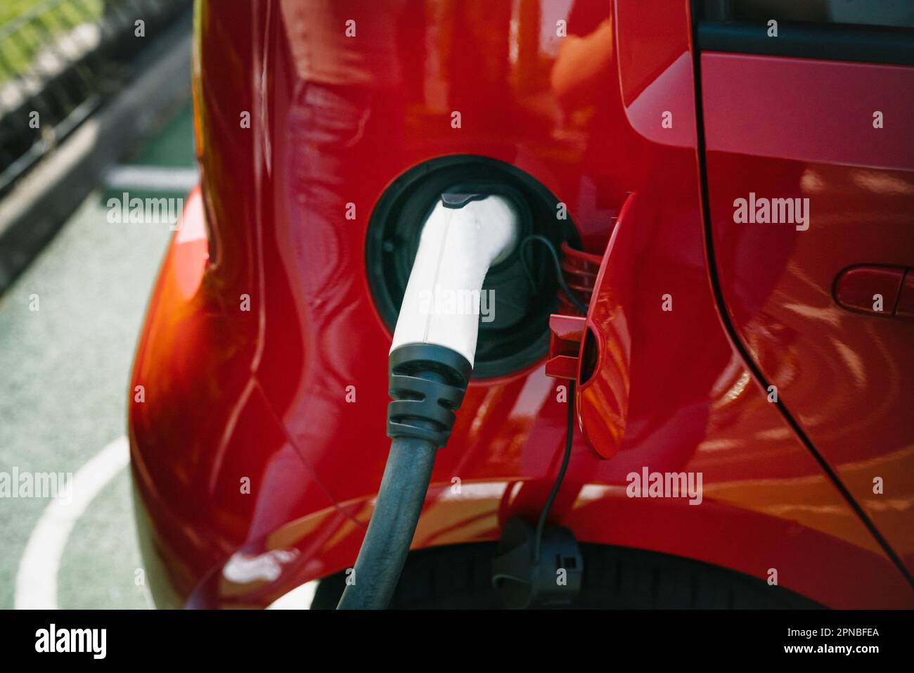Contemporary red electric car parked on asphalt road while charging ...