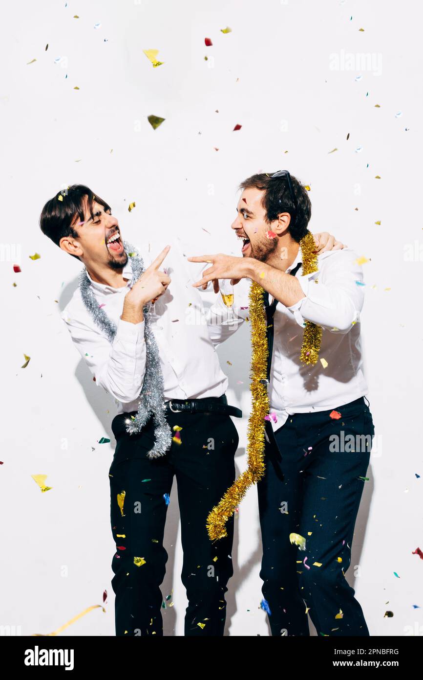 Drunk male partners in stylish wear with tinsels and alcoholic drinks ...