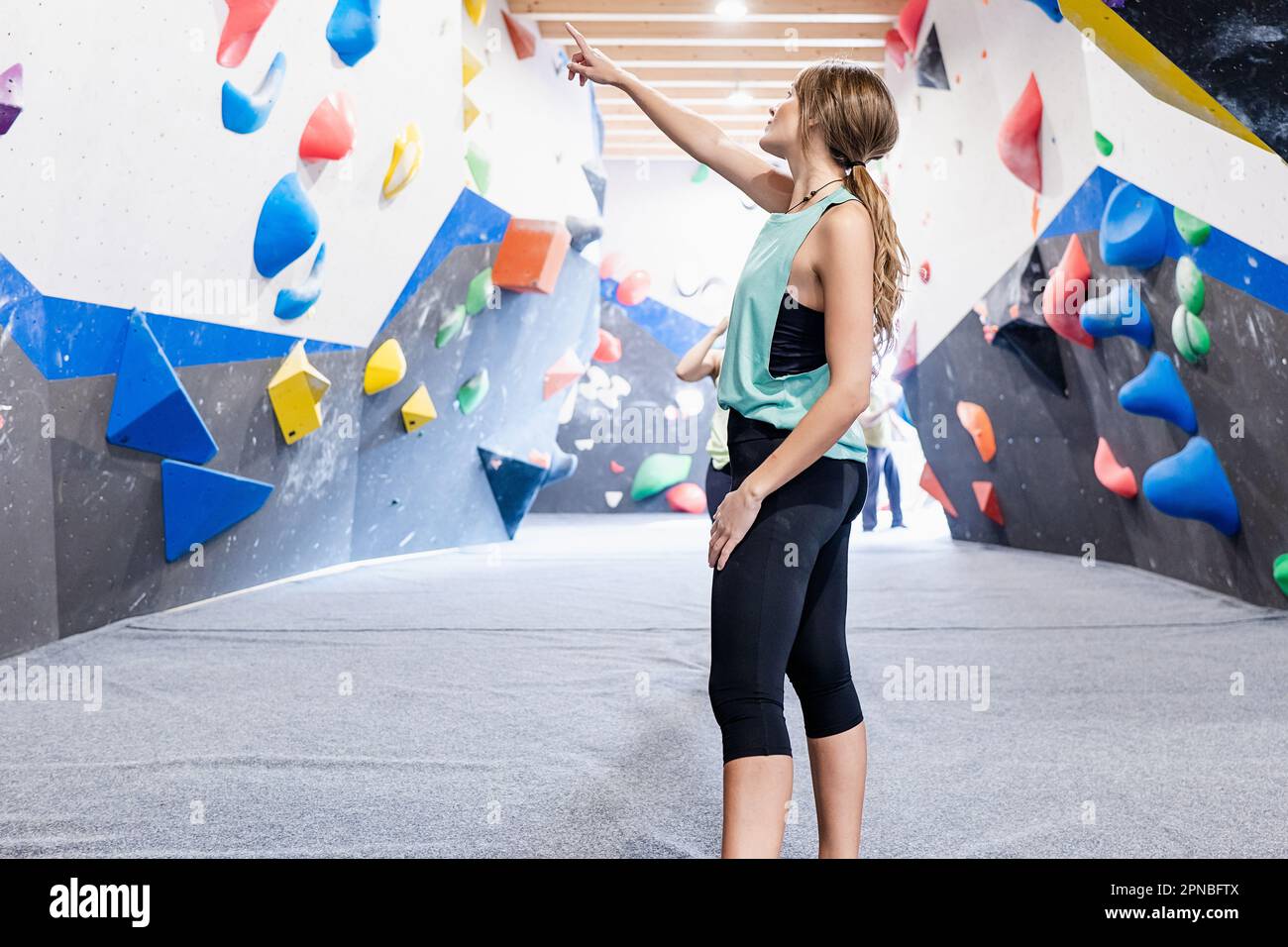Side view of young female standing near bouldering wall with color ...
