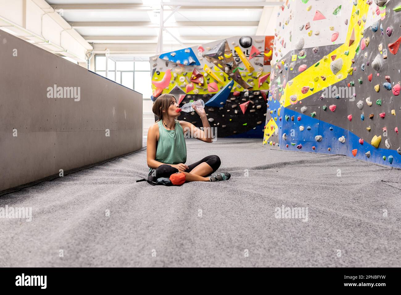 Side view of female climber relaxing with legs crossed and drinking ...