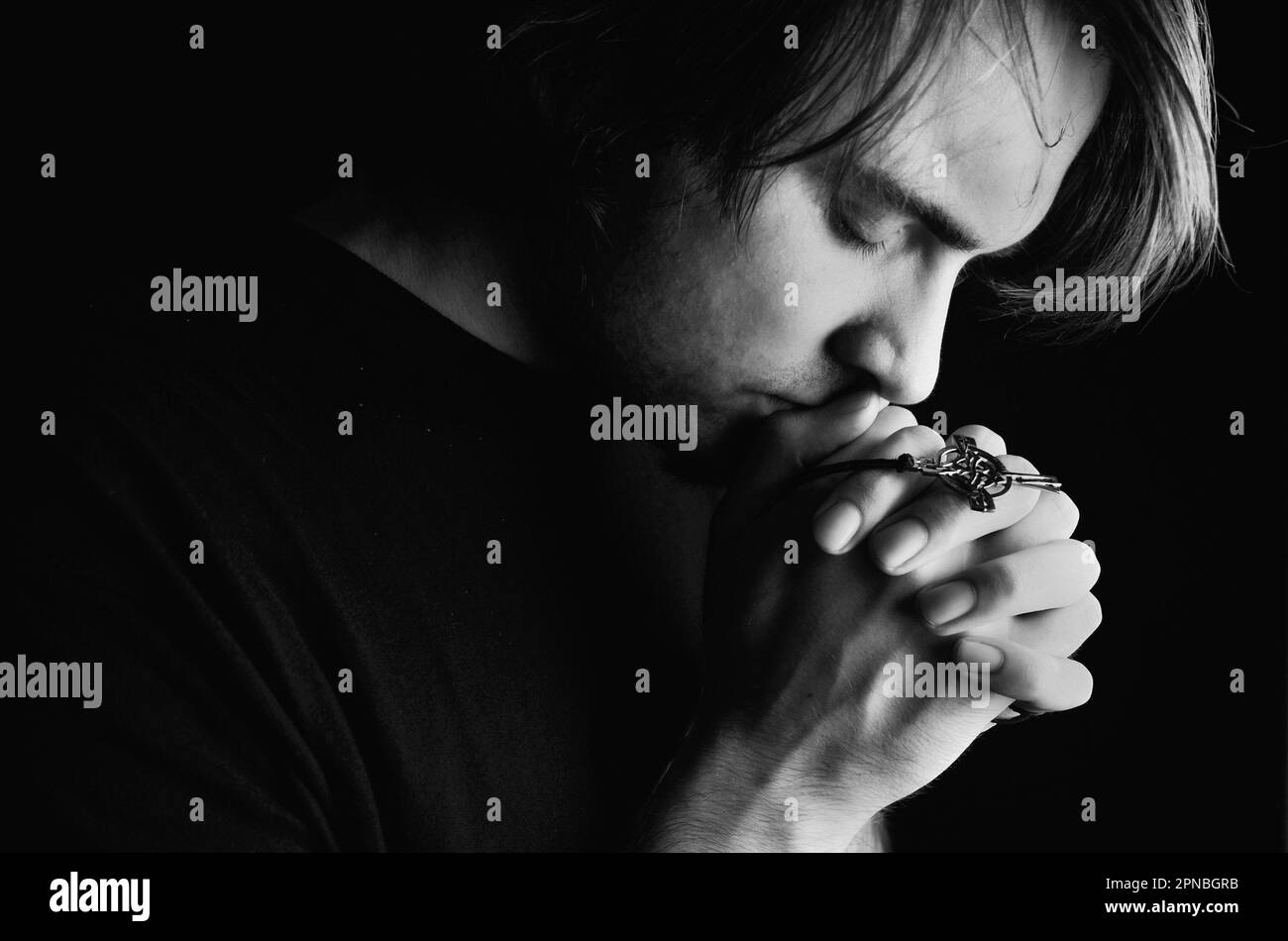Side view of young guy holding religious symbol in clasped hands and ...