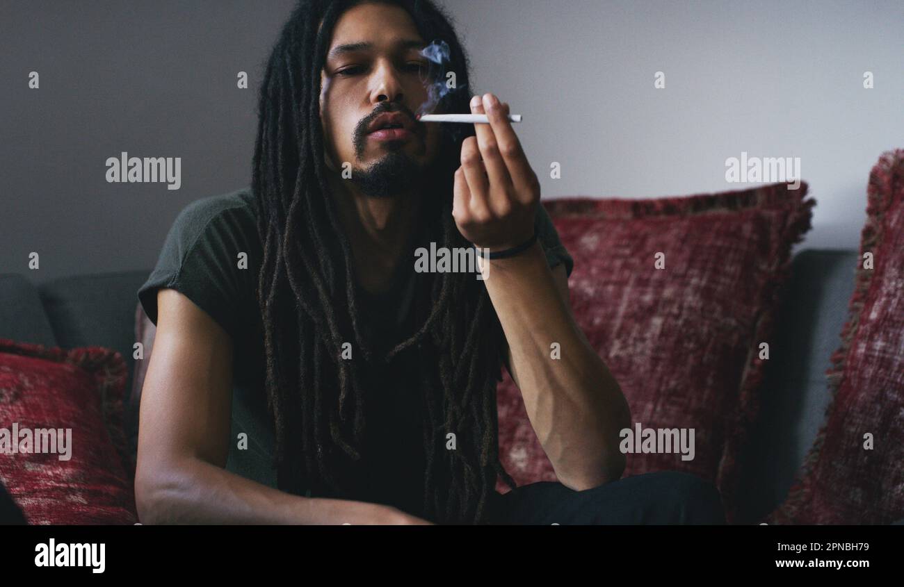 Under the influence. a young man smoking a marijuana joint at home ...