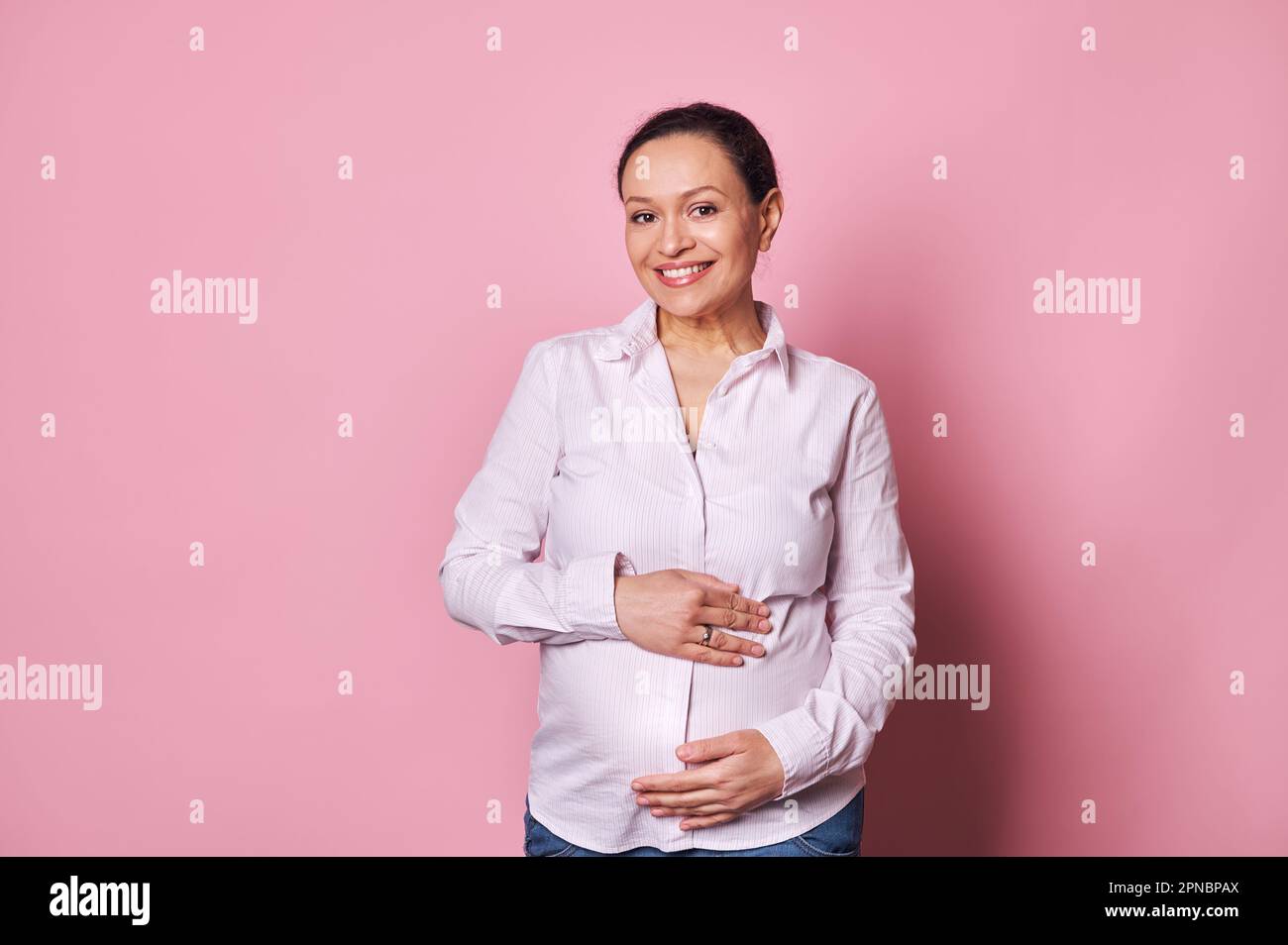 Middle aged pregnant brunette pretty woman holding hands on her belly ...