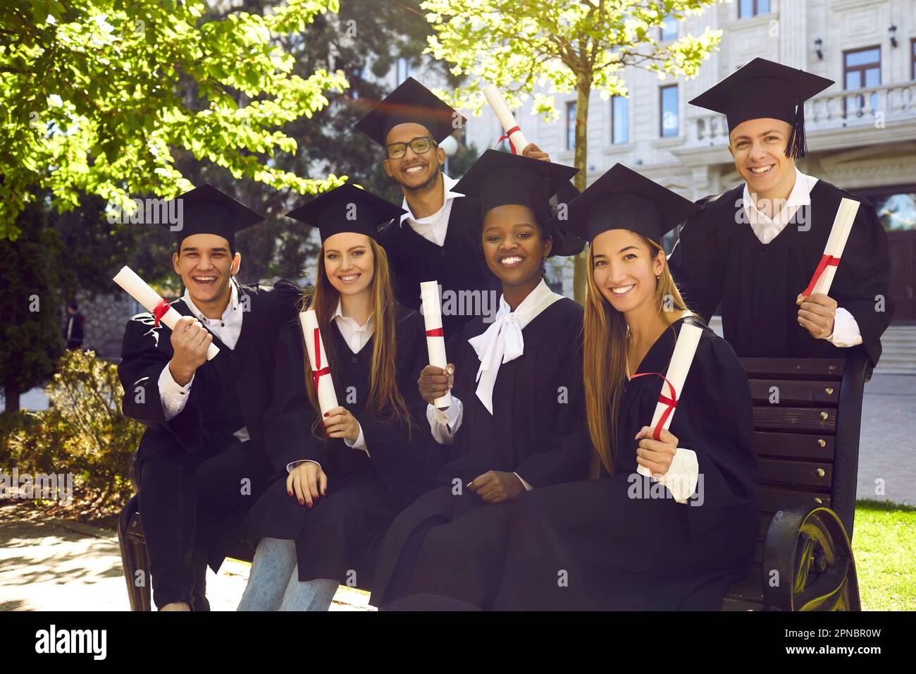 Happy group of multiracial people in graduation gowns with diplomas ...