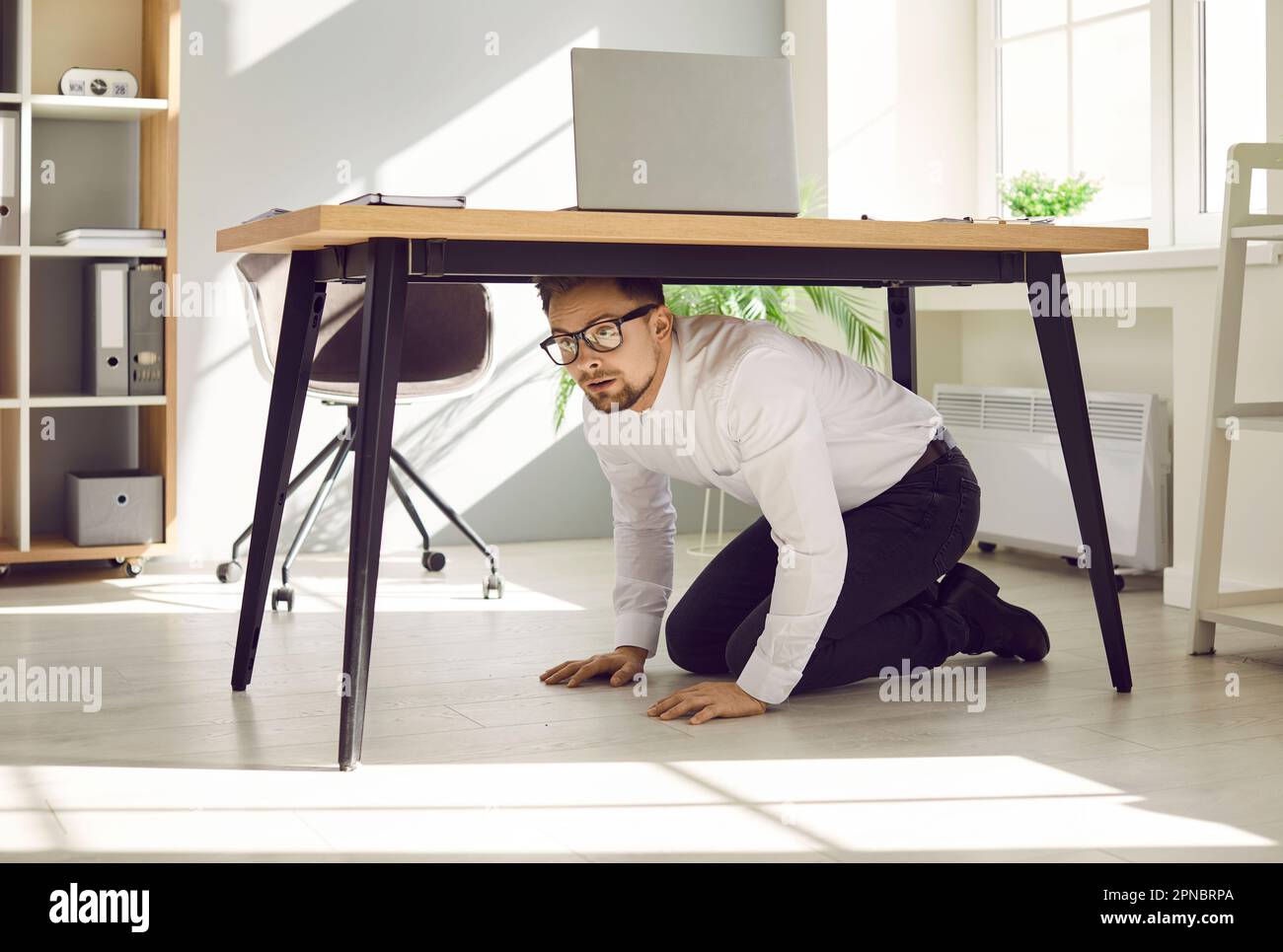 Portrait of a scared stressed young business man hiding under the desk ...