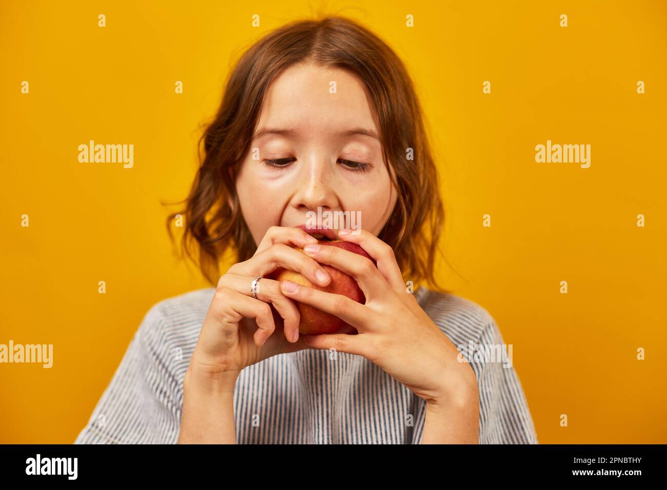 Pretty teen girl, child eat, bites a fresh red apple isolated on studio ...