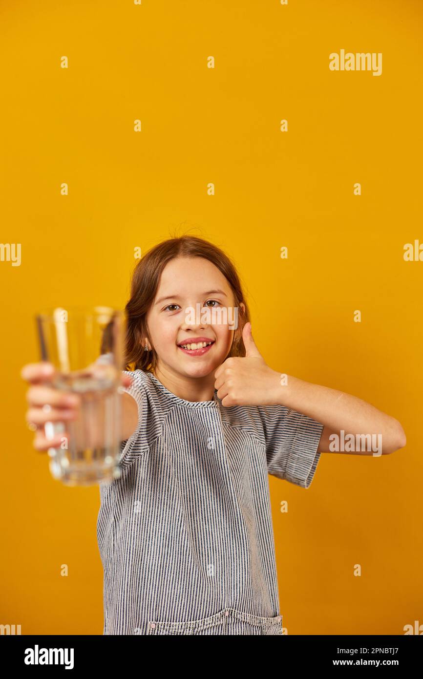 Pretty teen girl, child with a fresh glass of water, thumb up isolated ...