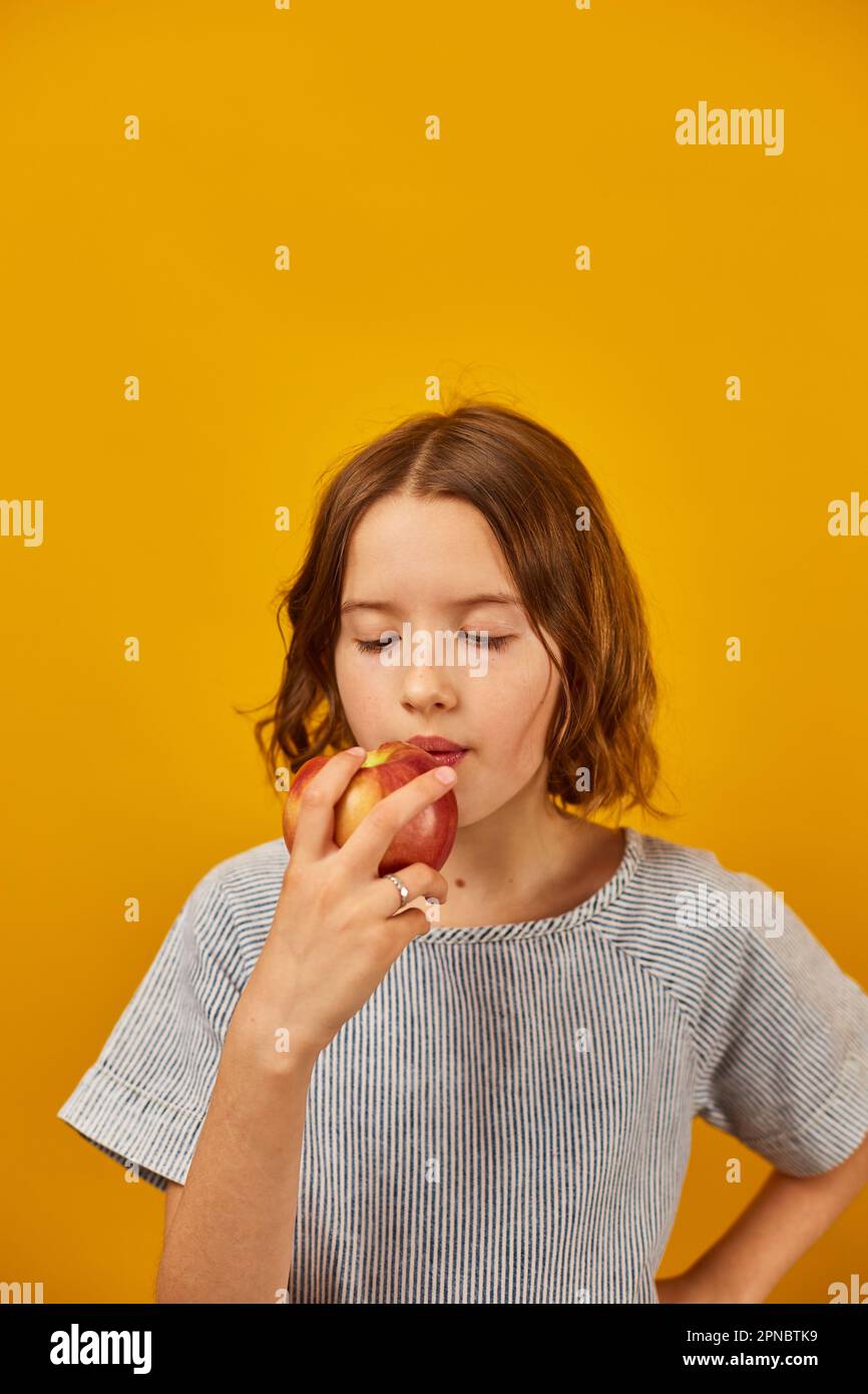 Pretty teen girl, child eat, bites a fresh red apple isolated on studio ...