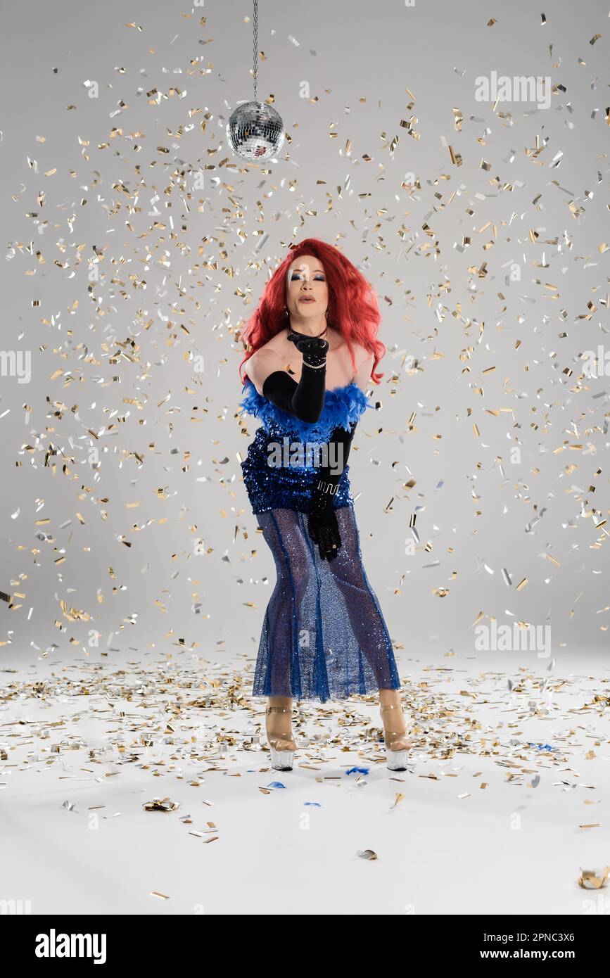 Elegant drag queen in dress and gloves blowing air kiss under disco ...