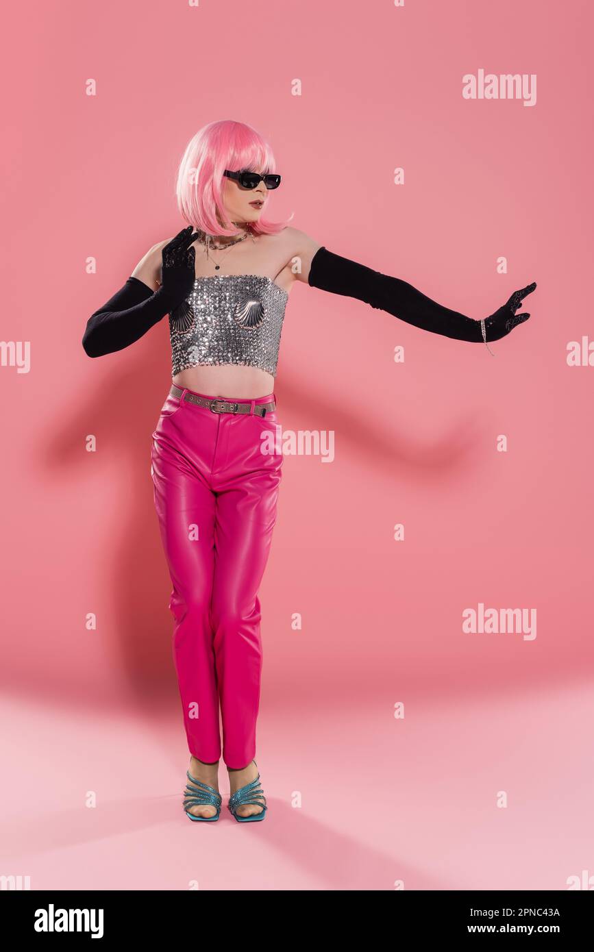 Full length of drag queen in sparkling top and gloves posing on pink ...