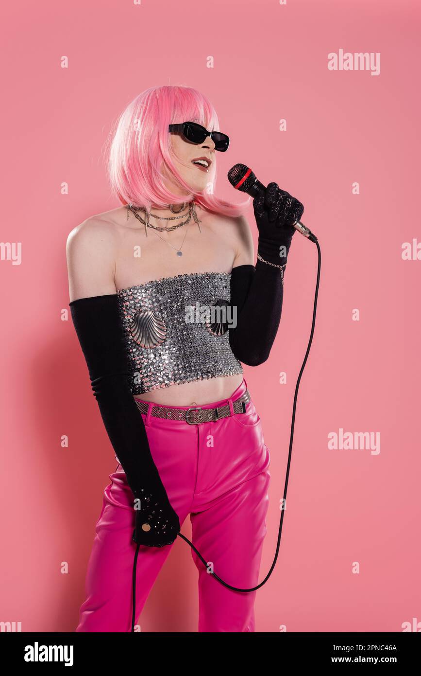 Drag queen in sunglasses and sparkling top holding microphone on pink ...