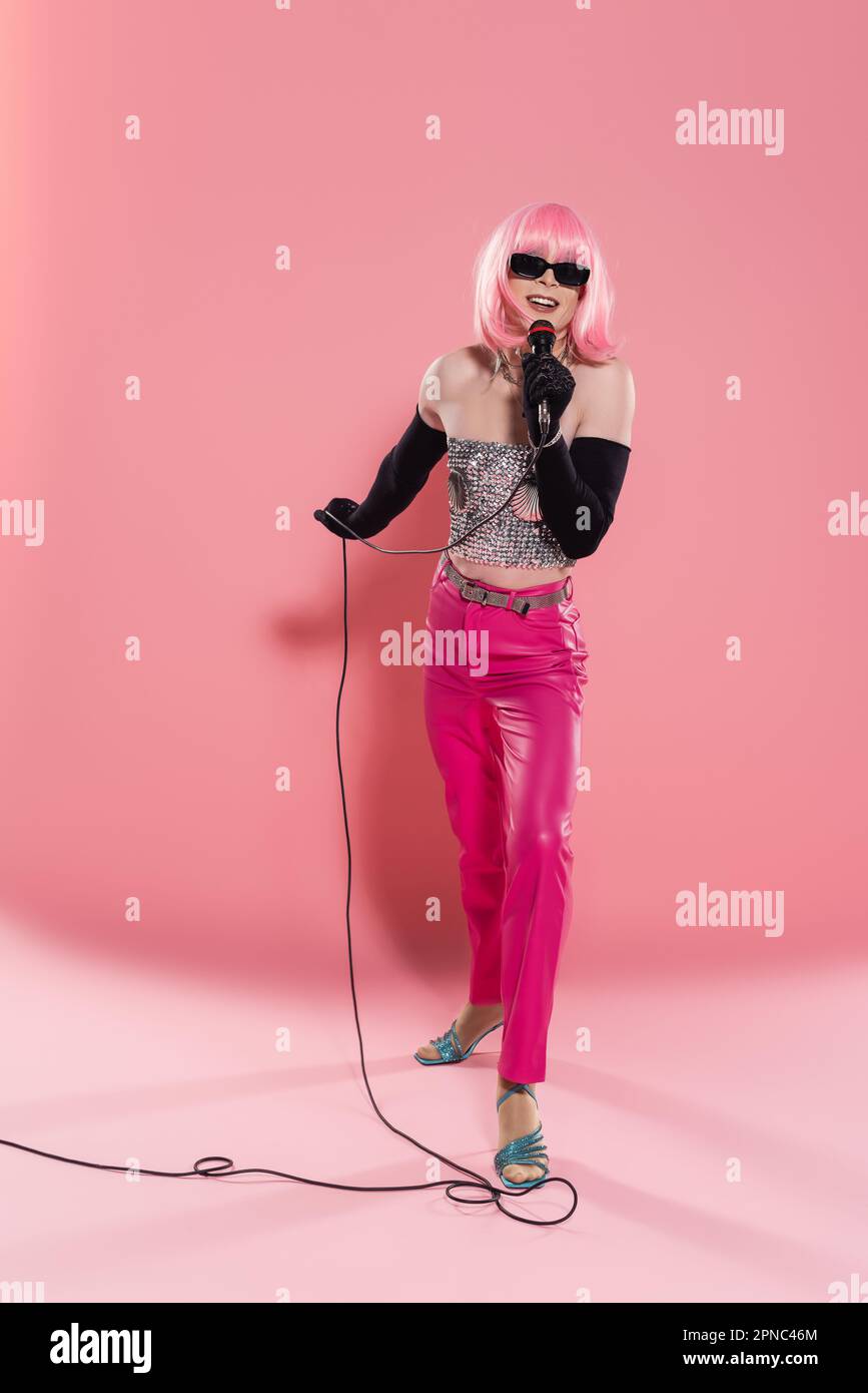 Full length of smiling drag queen in gloves and sunglasses holding ...