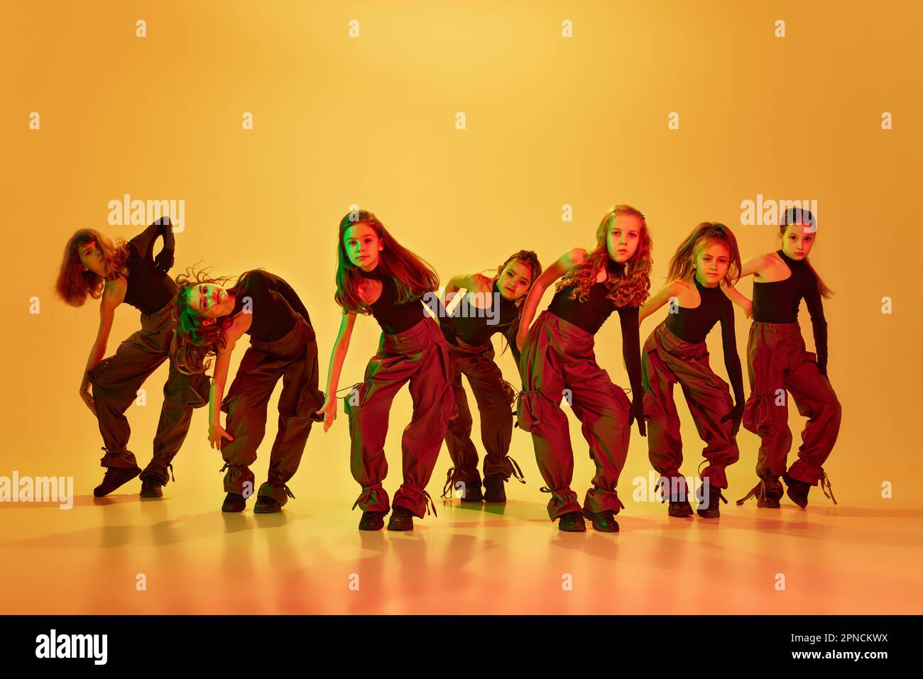 Expressive dance. Group of stylish little girls, kids, dancing, training hip-hop against yellow ...