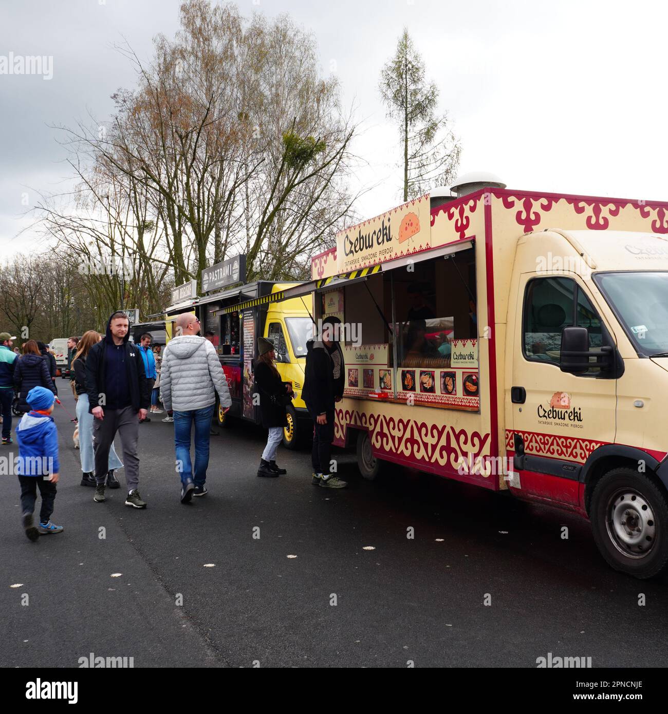 A large crowd of people is gathered around several parked delivery ...