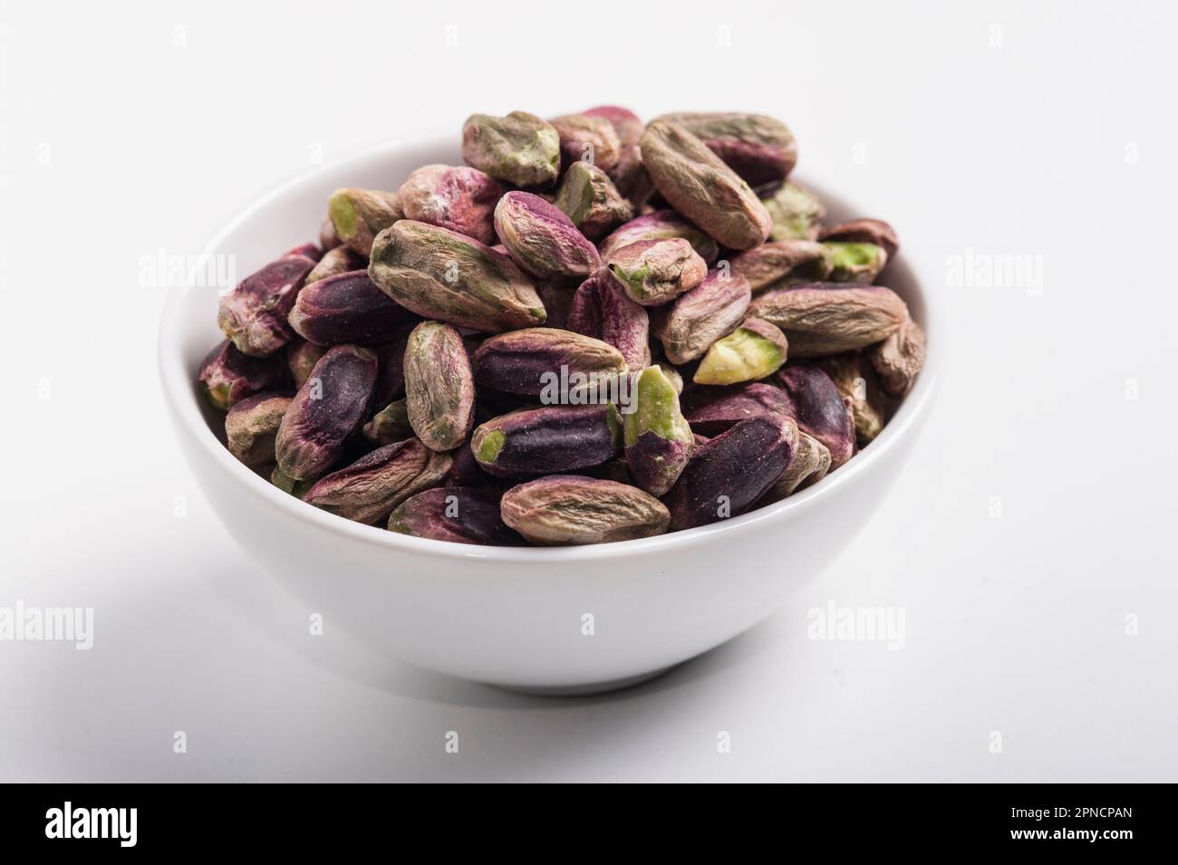 pistachio seeds in a small bowl on a white background Stock Photo - Alamy