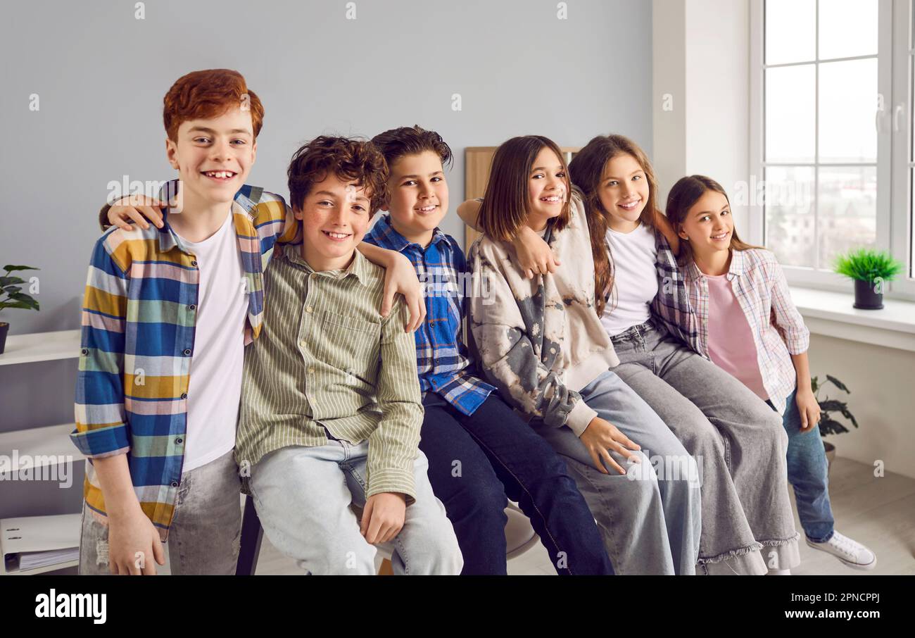 Group portrait of happy, hugging school friends sitting on a desk in ...