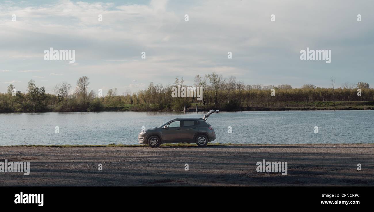 A car is parked in a scenic location by a lake, with the trunk open ...