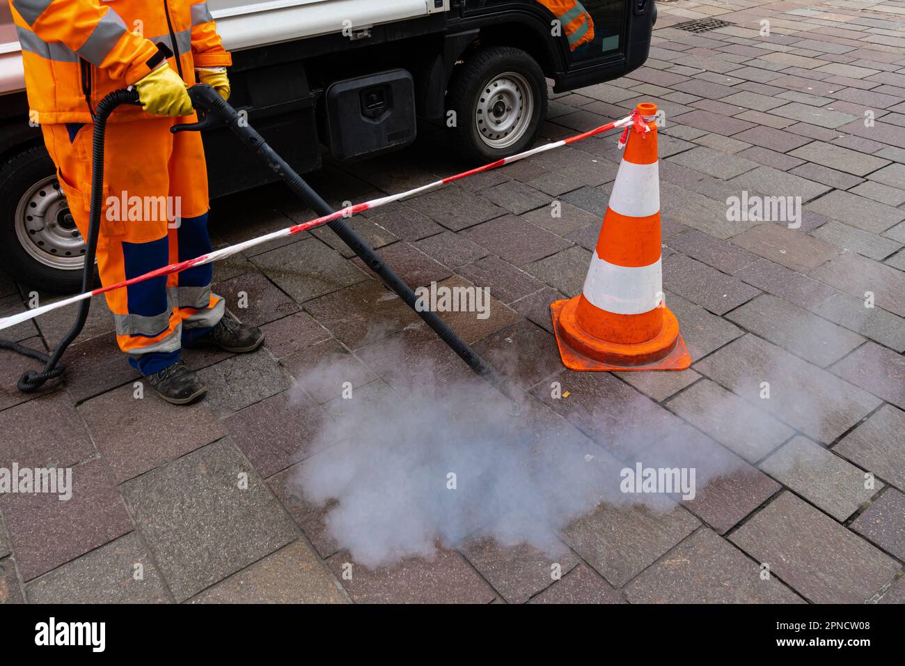 Road worker cleans the pavement with a steam pressure hose. Orange ...
